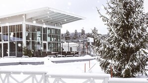 Um edifício moderno com grandes janelas, uma área de estar coberta ao ar livre e uma paisagem coberta de neve.