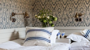 Uma cama bem arrumada com almofadas listradas, uma mesa de cabeceira com um vaso de flores e luminárias fixadas na parede.
