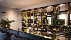 Uma área de bar com diversas garrafas de bebidas, um balcão de vidro e assentos.