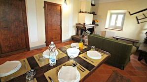 Uma área de refeições com uma mesa de madeira posta para quatro pessoas, um sofá estofado verde e uma lareira.