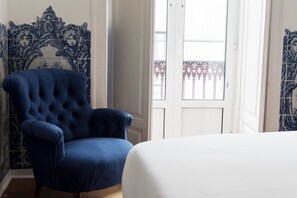 Quarto com poltrona estofada azul, cama branca e parede decorada com azulejos.