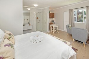 Quarto de hotel com cama, chuveiro, pequeno espaço de cozinha, janela com cortinas e área de estar.