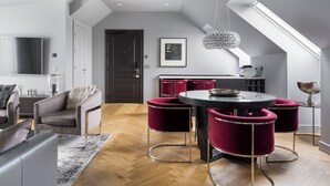 Um loft moderno com área de refeições com uma mesa redonda e cadeiras de veludo vermelho, sala de estar com sofá cinza e uma TV grande fixada na parede.