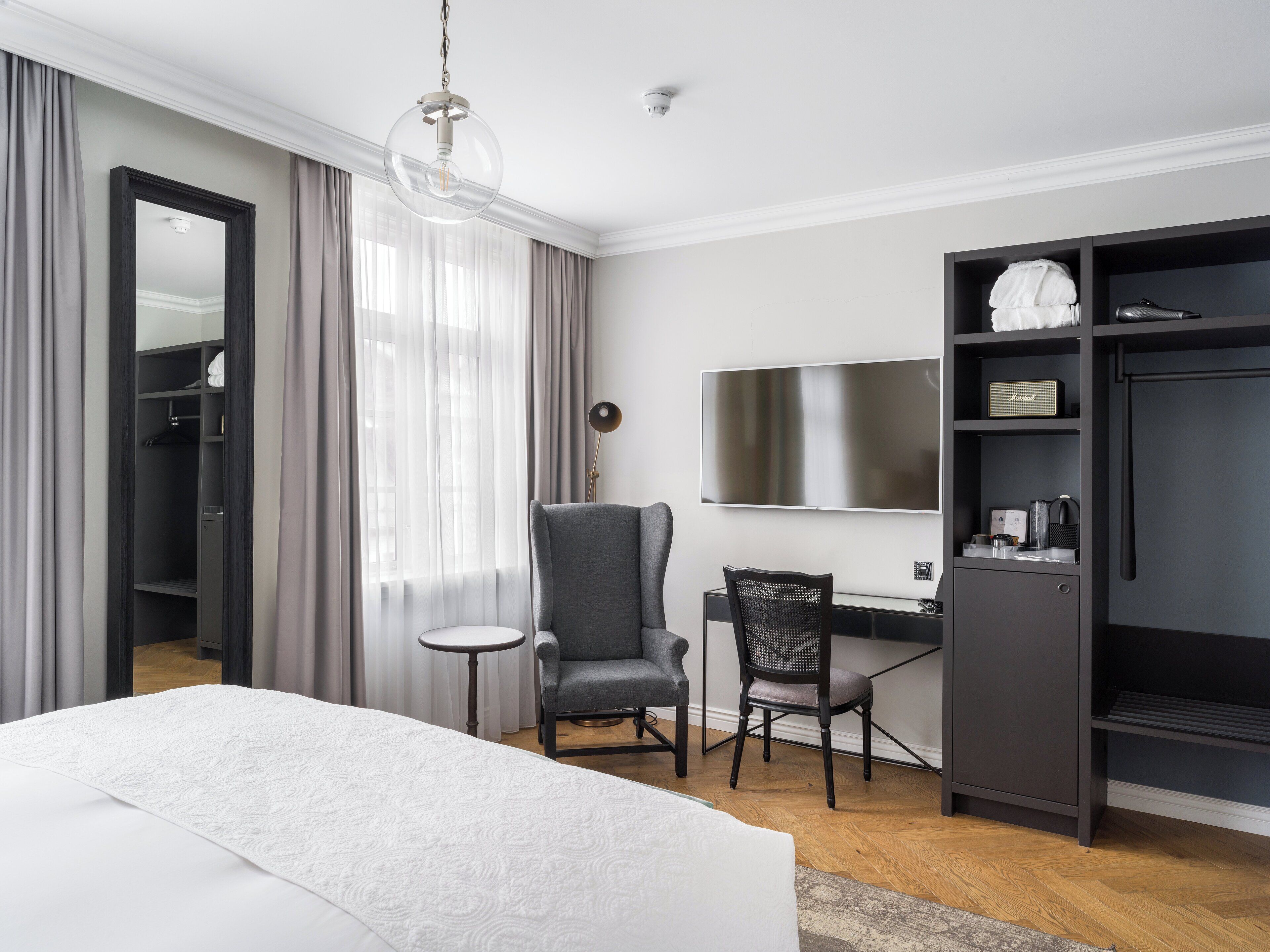 Quarto de hotel com cama, duas cadeiras, escrivaninha com televisão, guarda-roupa e uma pequena mesa.