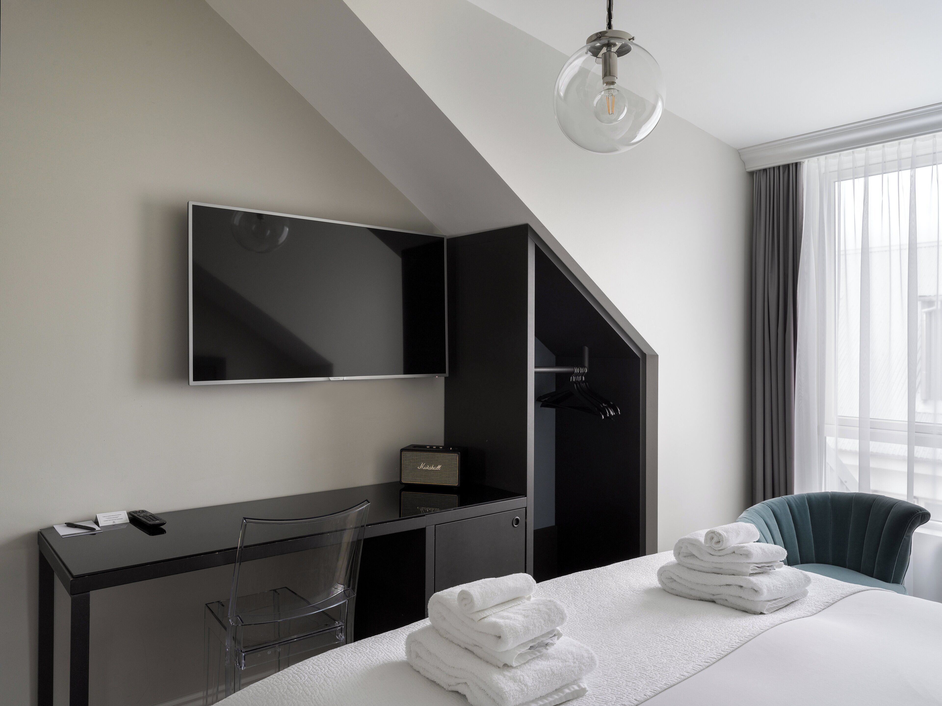 Quarto de hotel moderno com uma cama grande, uma escrivaninha com cadeira, televisão de tela plana, luminária pendente e vista da cidade pela janela.