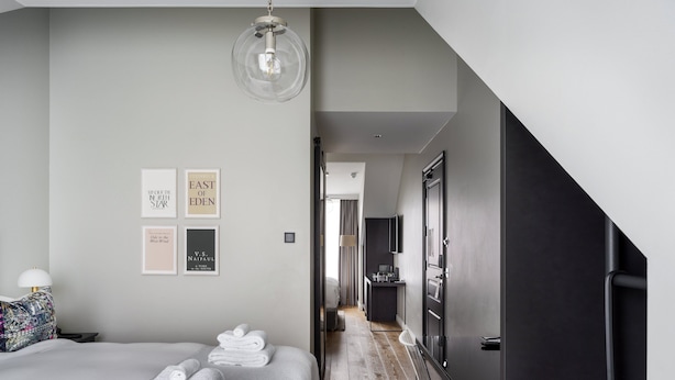 Quarto de hotel moderno com cama, escrivaninha, TV de tela plana e corredor que dá para um banheiro.