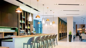 Uma área de bar moderna com um balcão comprido, banquetas e iluminação pendente.