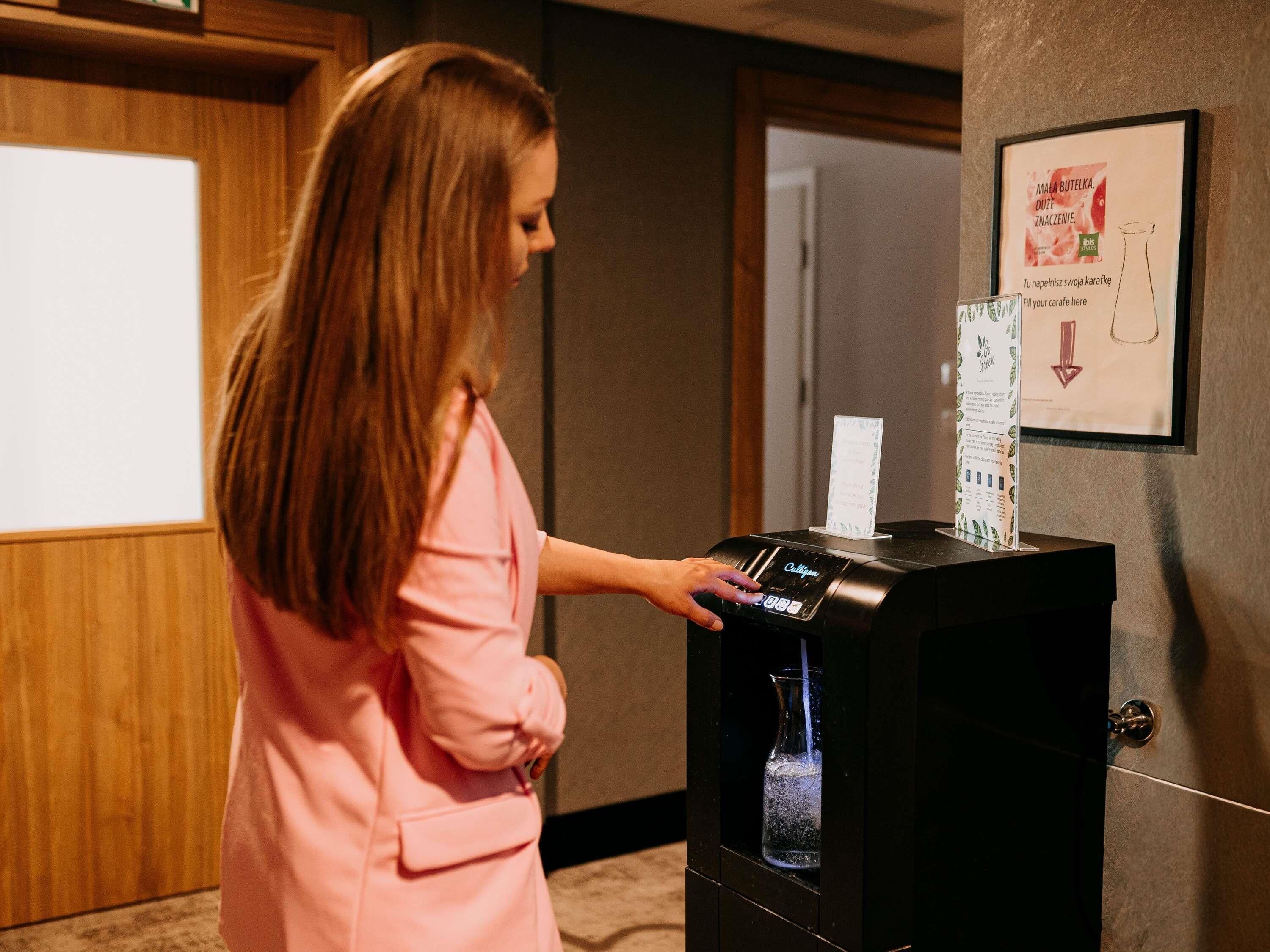 Pessoa utilizando um dispensador automático de bebidas em um quarto de hotel.