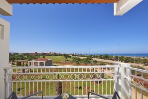 Uma varanda com vista para um campo de golfe e o mar.