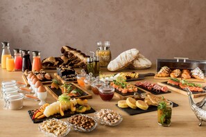 Diversos alimentos e bebidas sobre uma mesa de madeira, incluindo pão, doces e acompanhamentos.