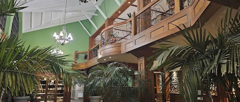 Um amplo átrio com pé-direito alto, escada de madeira e muitas plantas.