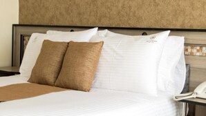 Quarto de hotel com cama, manta marrom, almofadas brancas e telefone branco em uma mesinha de cabeceira.
