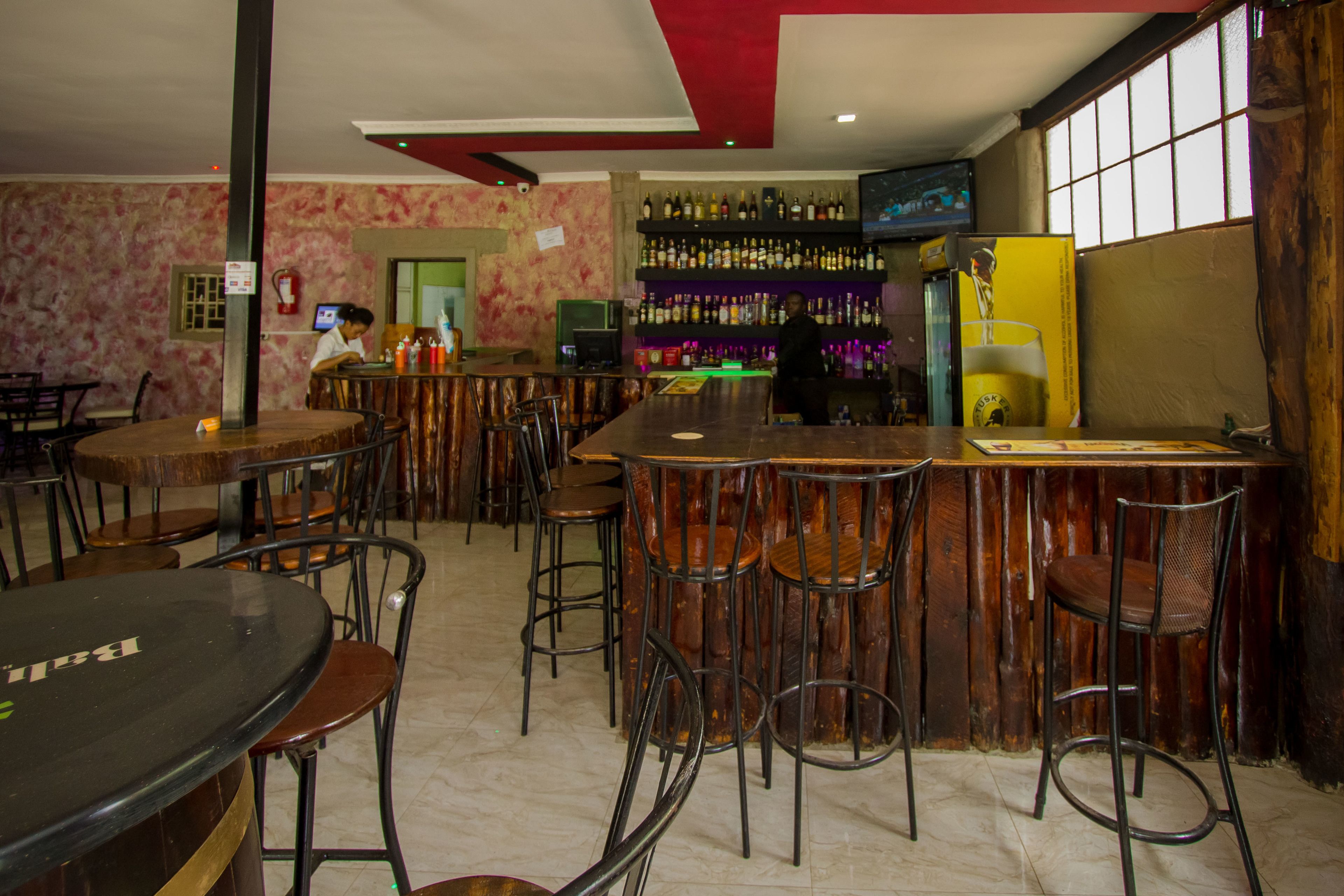 Uma área de bar com várias mesas e cadeiras, um balcão e prateleiras cheias de garrafas.