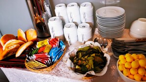 Buffet de café da manhã com canecas, pratos, pão e uma cesta de canetas coloridas.