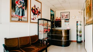 Uma área de recepção com um banco de couro marrom, uma vitrine de vidro com figurines e obras de arte emolduradas nas paredes.