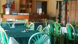 Restaurante com cadeiras e mesas verdes, área de bar com garrafas e vista para a rua.