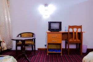 Quarto de hotel com secretária de madeira, televisão, cadeira, cama e tapete listrado.