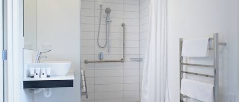 Um banheiro moderno com chuveiro, barras de apoio, porta-toalhas e pia com produtos de higiene pessoal.