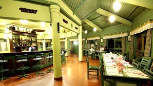 Um restaurante com área de bar, cadeiras verdes e mesas postas para refeições.