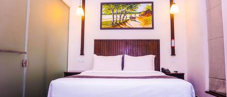 Quarto de hotel com cabeceira de madeira, um quadro com cena rural, abajur e telefone na mesa de cabeceira.