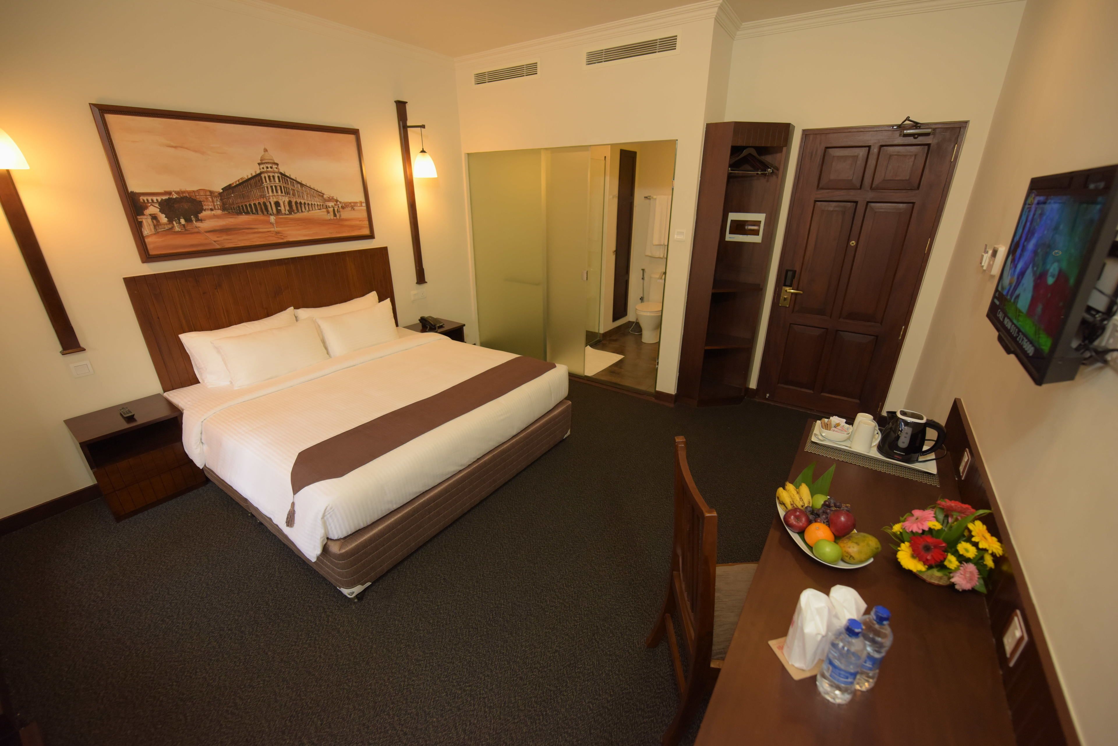 Quarto de hotel com cama, escrivaninha com fruteira, máquina de café e televisão.