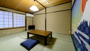 Quarto japonês tradicional com tatames, uma mesa de madeira baixa, um almofada azul, uma televisão e um grande cartaz na parede.