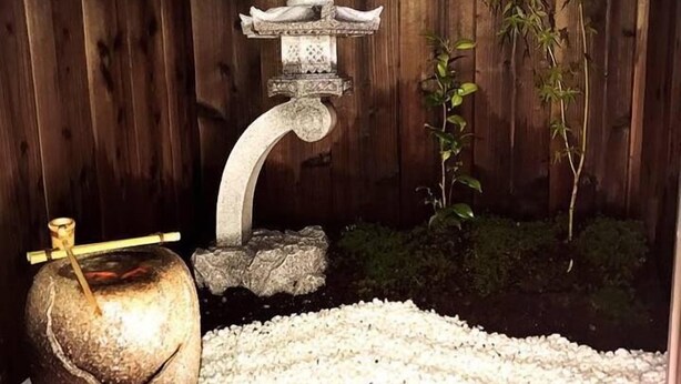Um jardim japonês tradicional com um lampião de pedra, uma grande bacia rochosa e plantas de bambu.