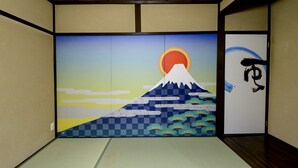 Um espaço com esteiras de tatame e pintura mural tradicional japonesa retratando o Monte Fuji e uma cerejeira.