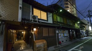 Uma rua estreita com arquitetura tradicional japonesa, incluindo um portão de madeira e um edifício com uma grande janela.