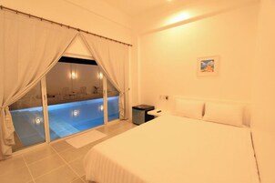 Quarto com uma cama grande, vista para uma piscina interior e uma pequena mesa de cabeceira.