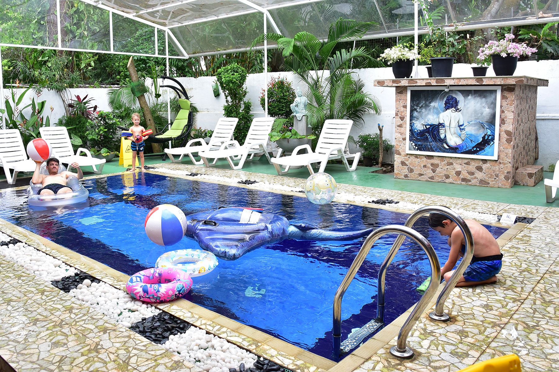 Piscina com brinquedos infláveis, cadeiras de descanso e uma estátua.