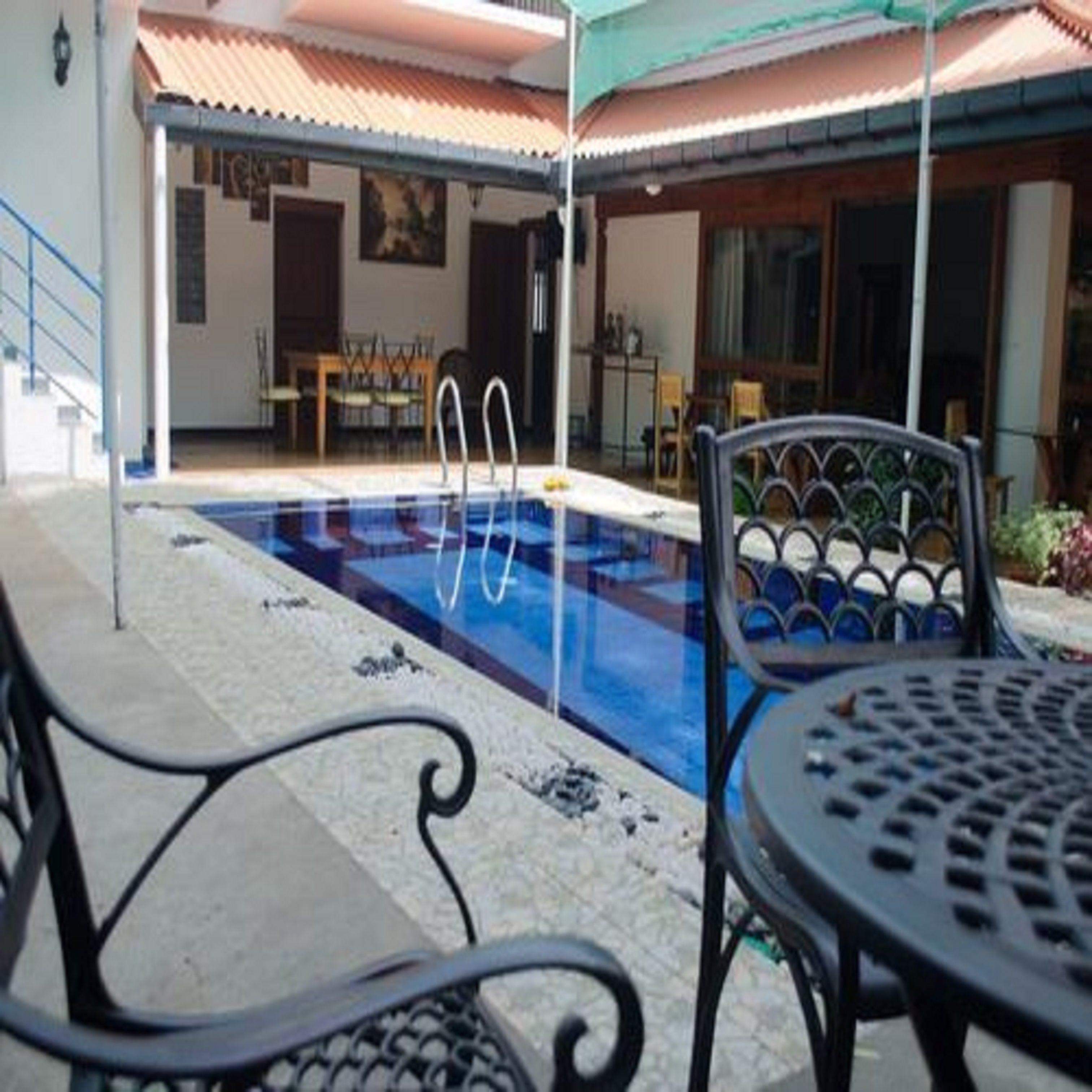 Piscina ao ar livre com área de estar coberta, incluindo uma mesa e cadeiras.