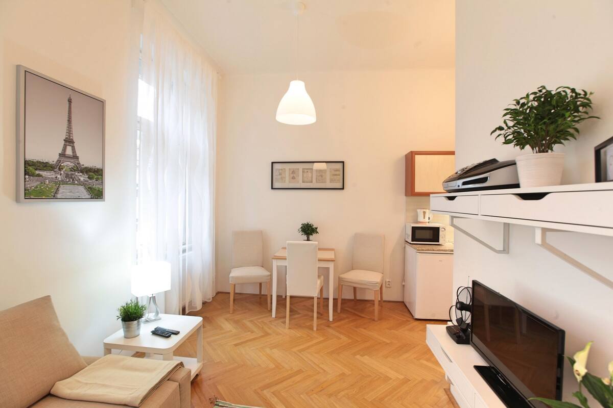 Uma sala de estar moderna com sofá, mesa de jantar com cadeiras, televisão, micro-ondas e um vaso de planta.
