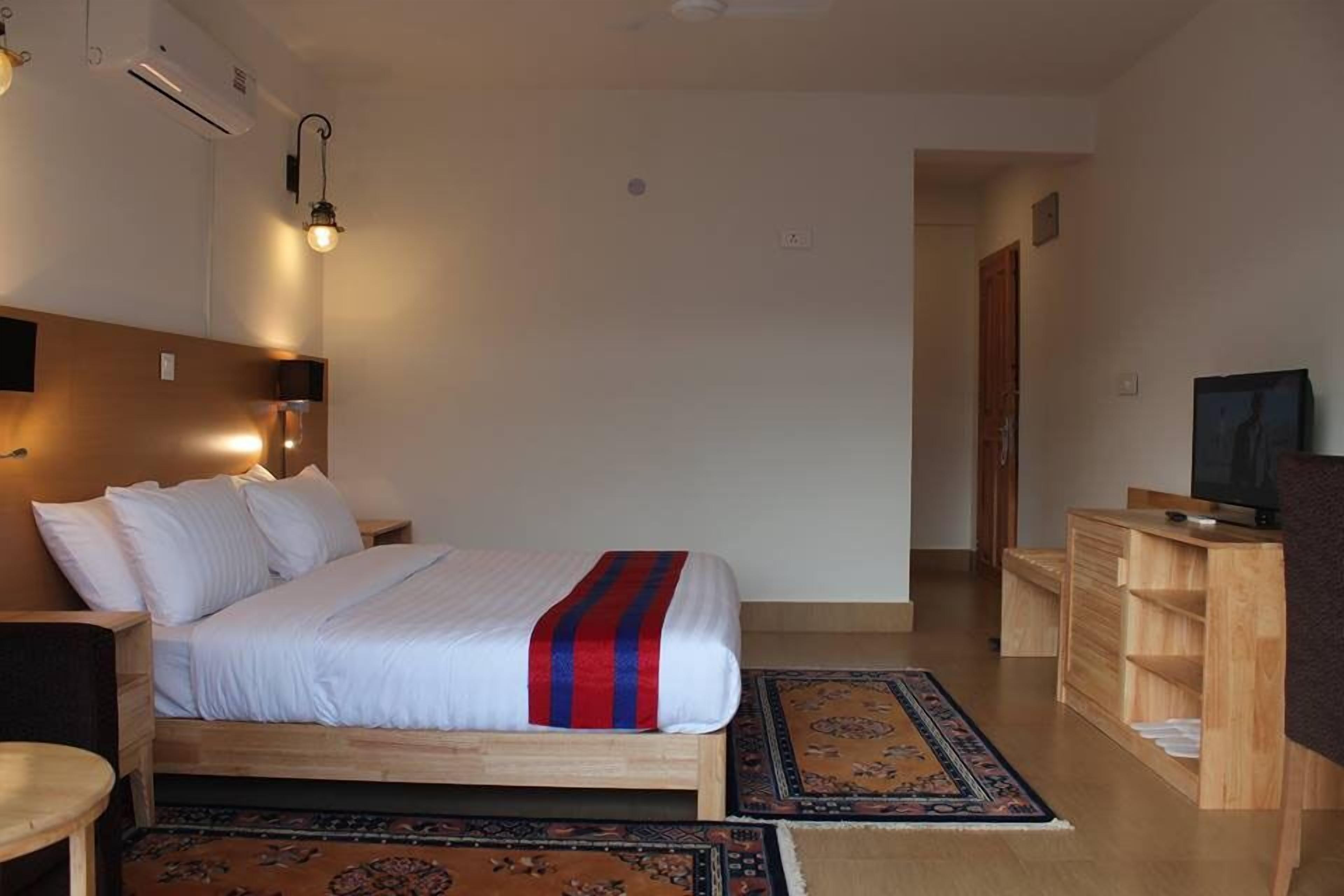 Quarto de hotel com cama, televisão, escrivaninha e cadeira.
