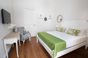 Quarto com uma cama, mesa de cabeceira, cadeira, televisão e porta.