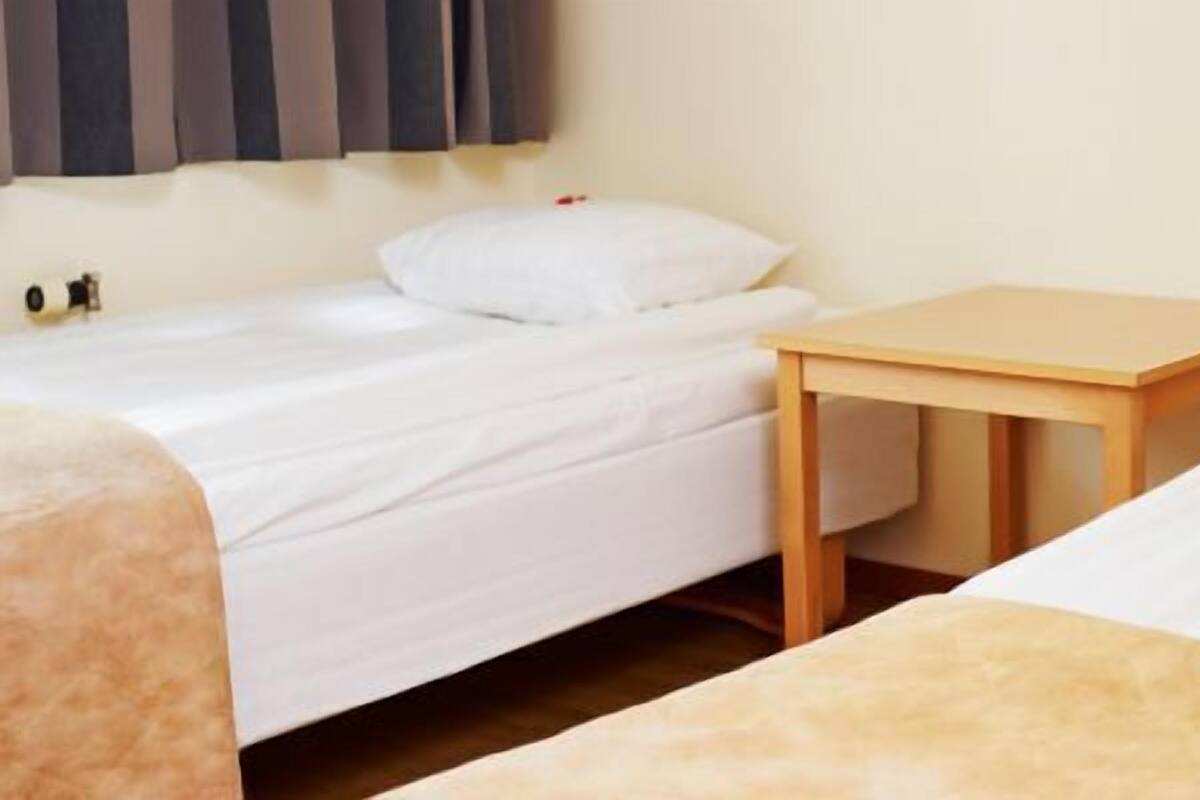 Quarto de hotel com duas camas de solteiro, uma mesa de cabeceira de madeira e uma pequena mesa.