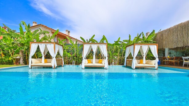 Uma piscina com três espreguiçadeiras brancas e toldos.