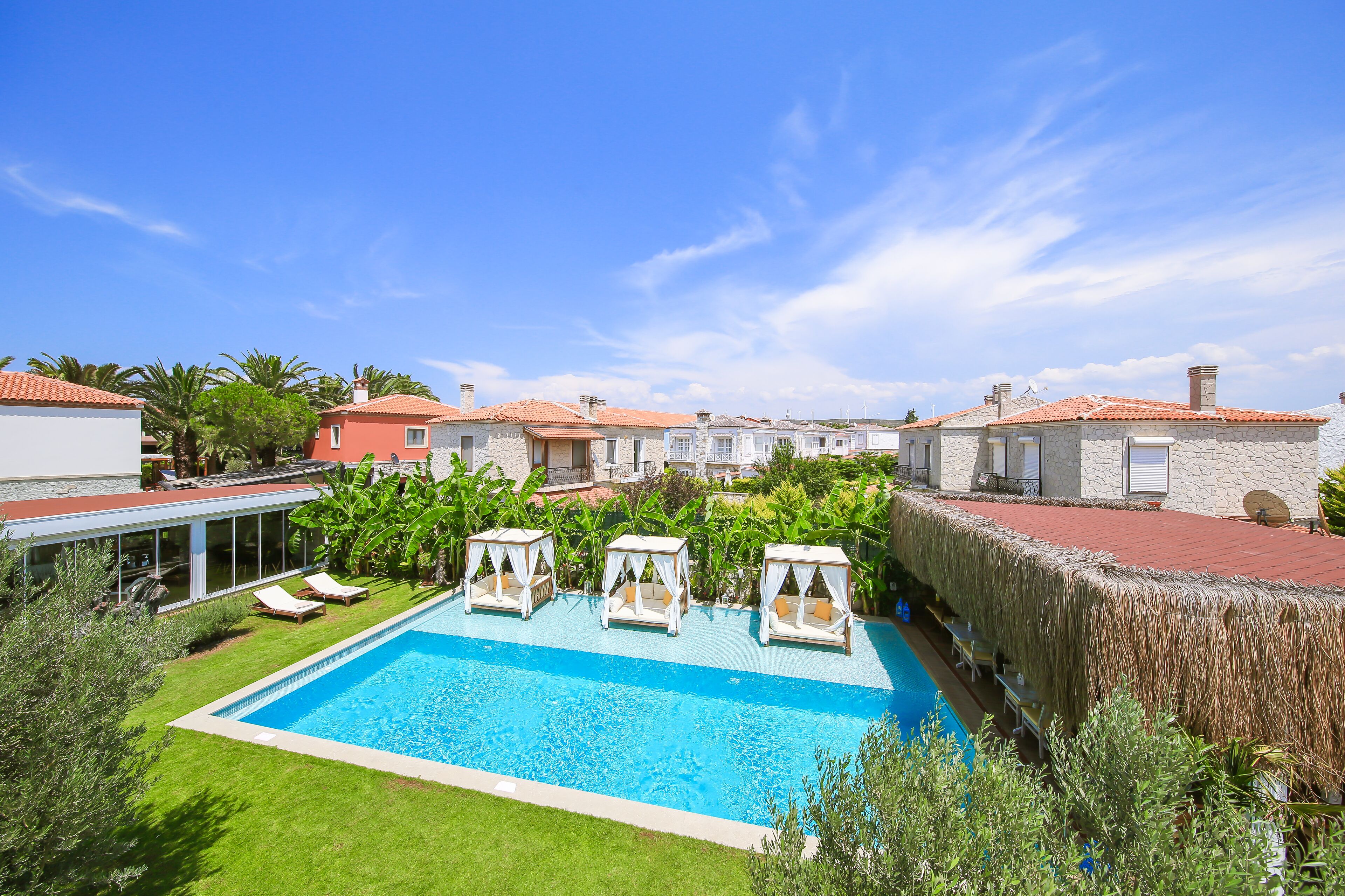 Piscina com espreguiçadeiras, cercada por vegetação e edifícios.