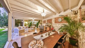 Uma ampla sala de jantar com uma longa mesa de madeira, rodeada por cadeiras modernas, um lustre e um vaso de planta.