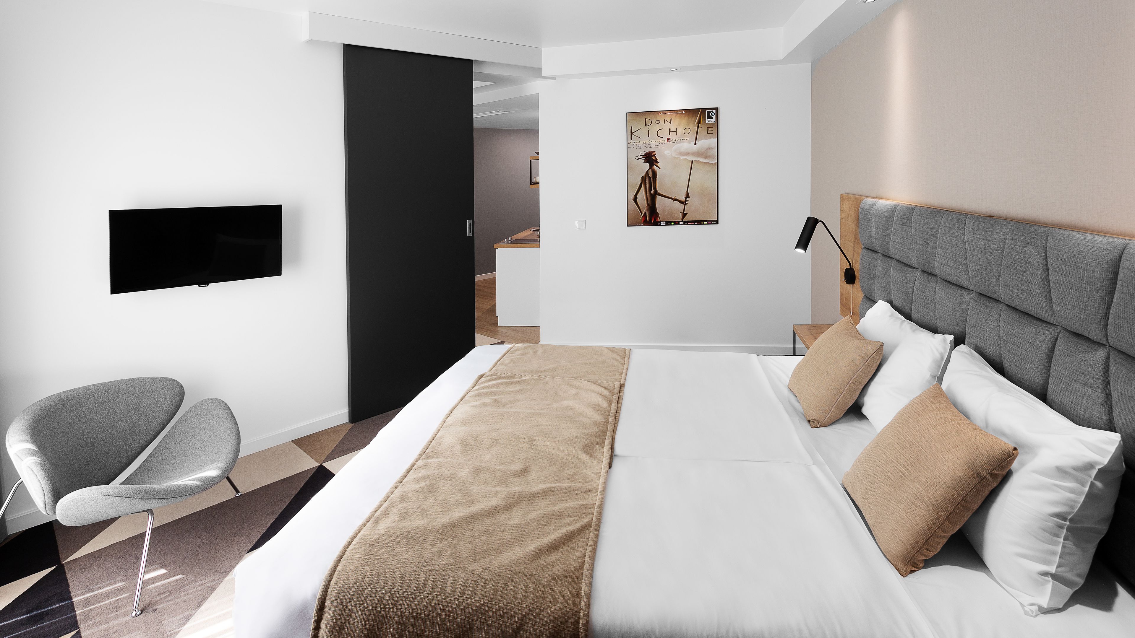 Quarto de hotel moderno com uma cama grande, televisão de tela plana, área de estar com uma cadeira e um quadro na parede.