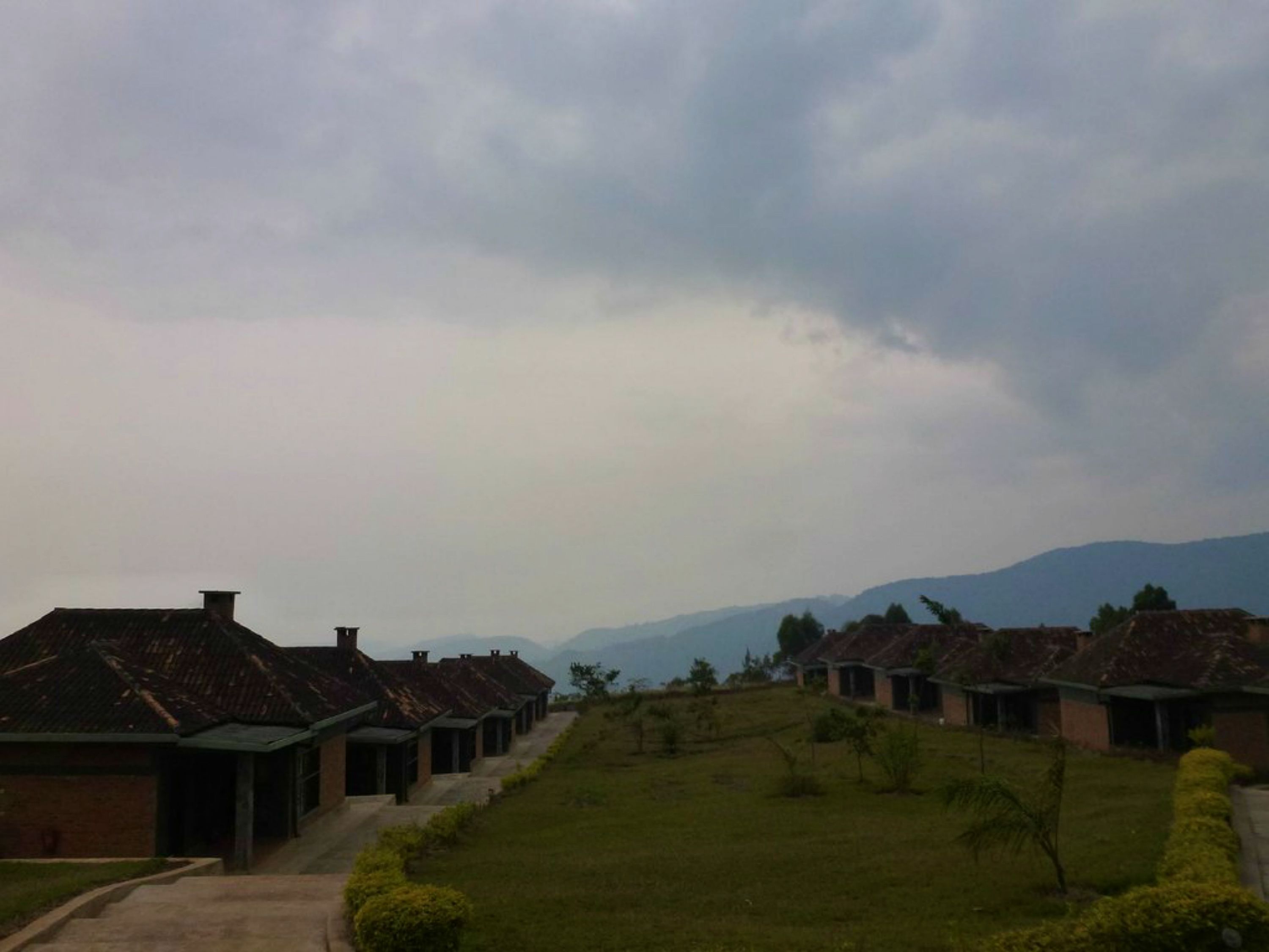 Fileira de edifícios em estilo tradicional com um pátio ajardinado e montanhas ao fundo.