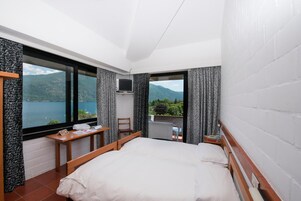 Quarto de hotel com uma cama grande, uma escrivaninha, uma cadeira, uma televisão e vista para um lago e montanhas.