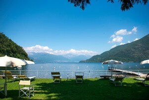 Vista para o lago com cadeiras de lounge e guarda-sóis, um píer e montanhas ao fundo.