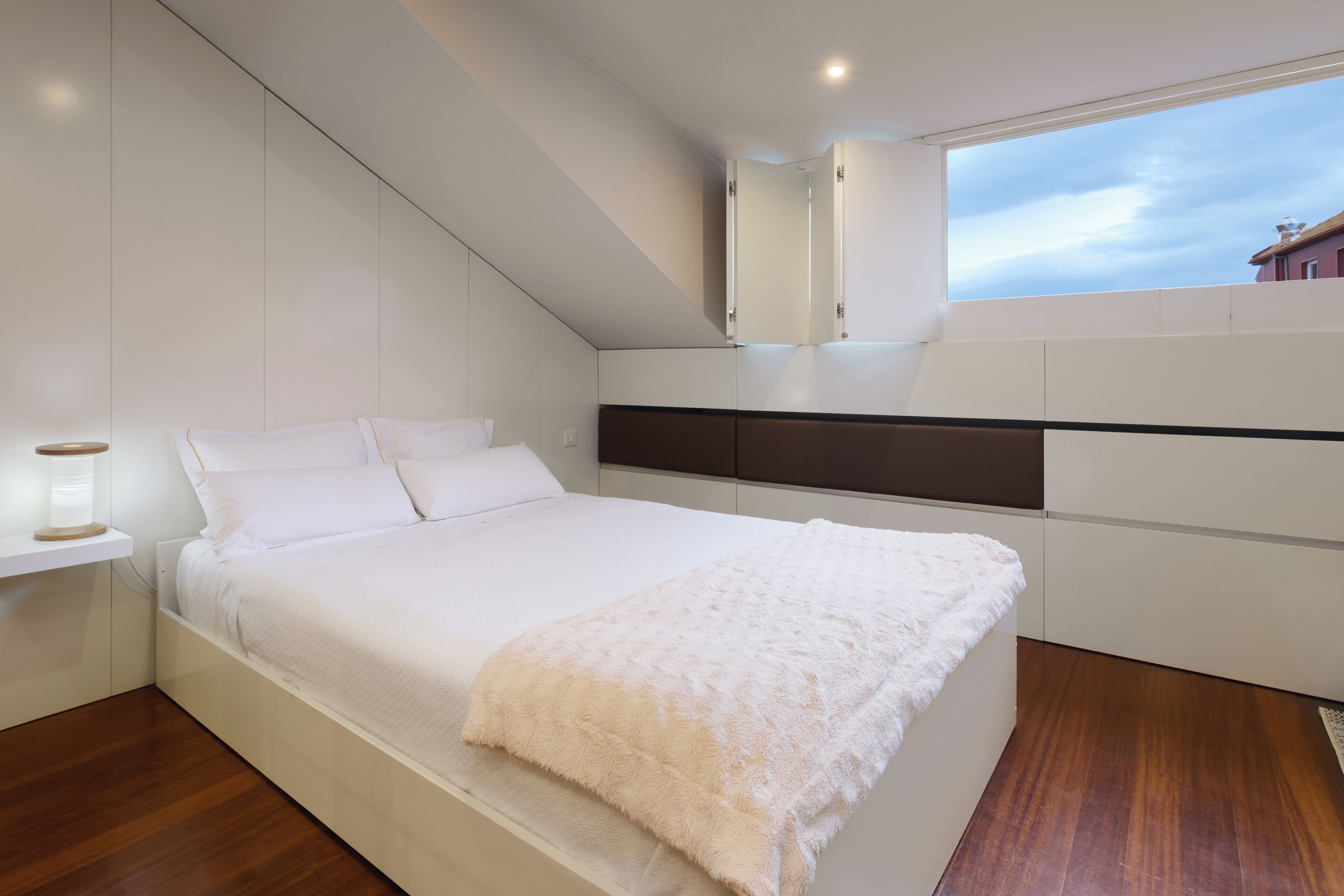Quarto moderno com cama grande, espaço de armazenamento embutido e claraboia.