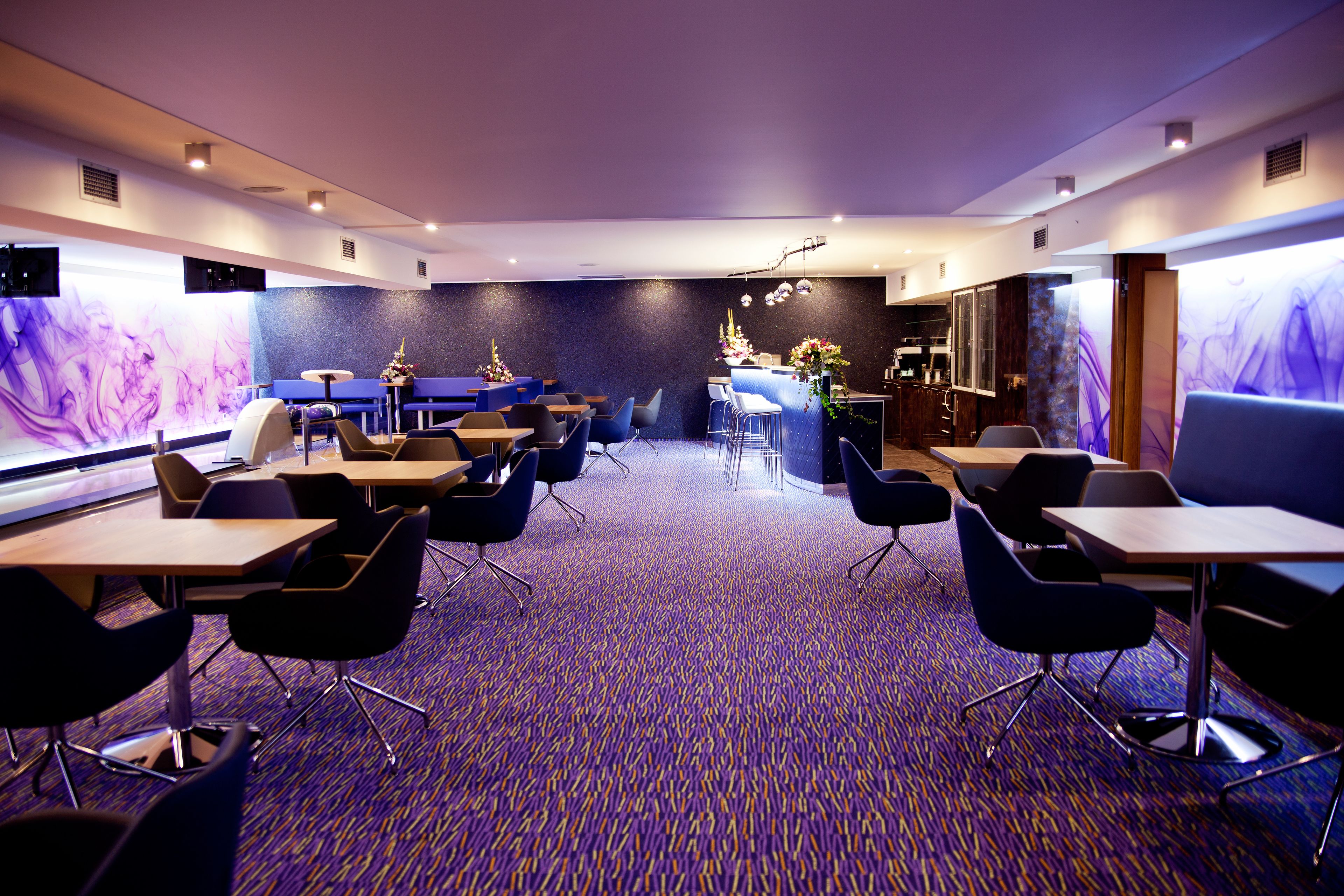 Um hall de hotel moderno com carpete roxo, várias áreas de estar e um bar.