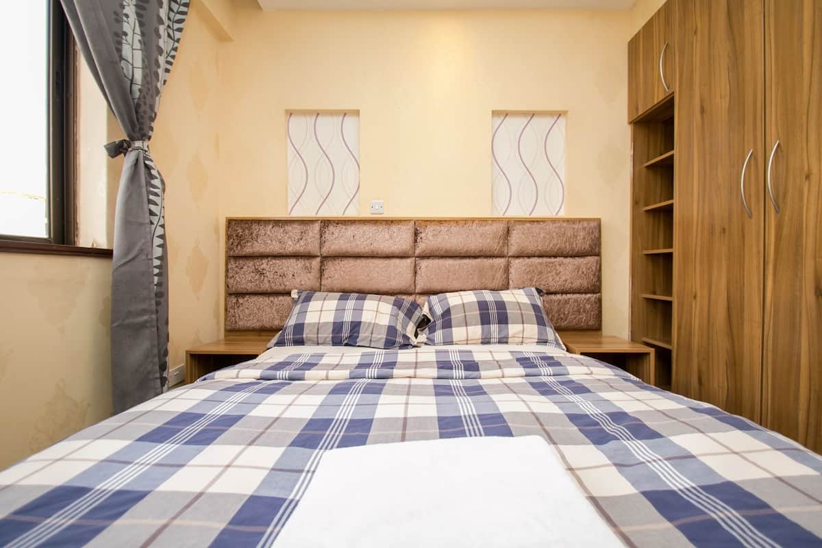 Quarto com cama, cabeceira, guarda-roupa e cortinas.