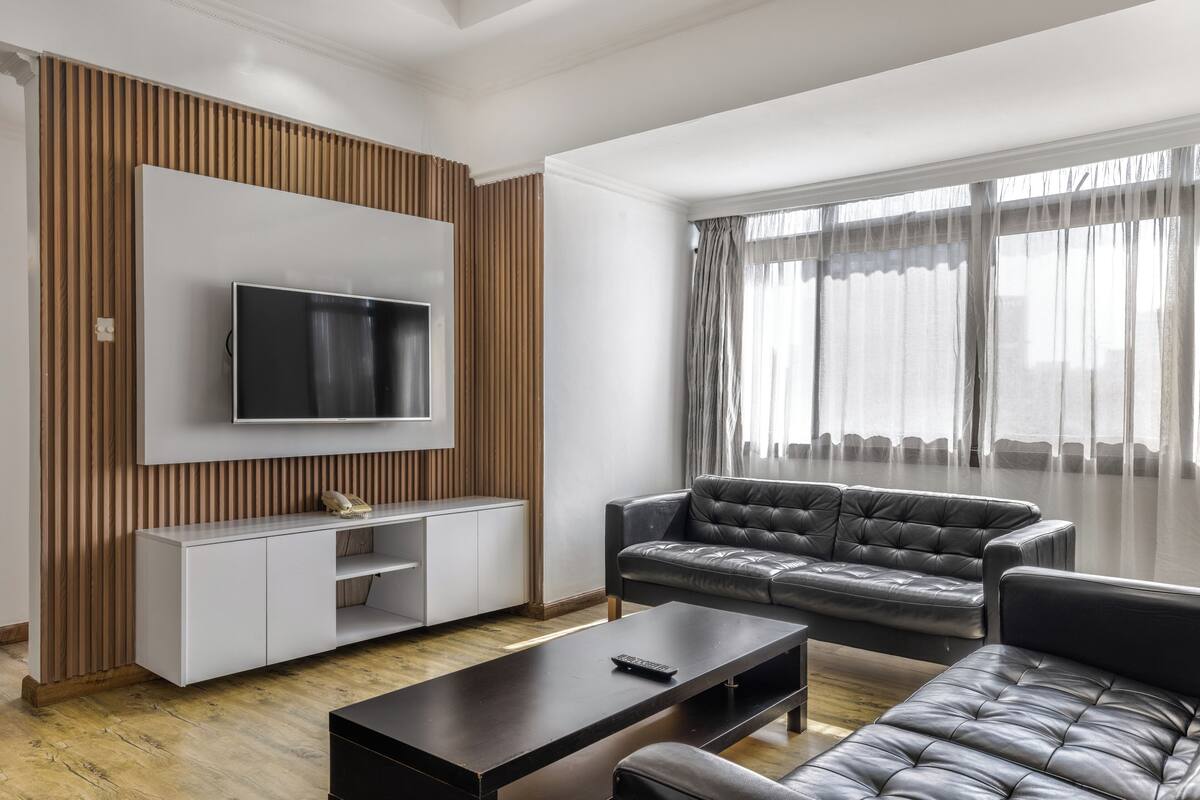 Uma sala de estar moderna com uma TV de tela plana presa a uma parede branca, um sofá de couro, uma mesa de centro e uma parede de destaque em madeira.