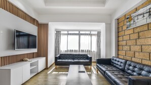 Uma sala de estar moderna com um sofá de couro preto, uma televisão de tela plana e uma parede de destaque em tijolo.