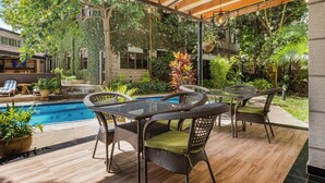 Um pátio externo com piscina, móveis de vime e vegetação exuberante.