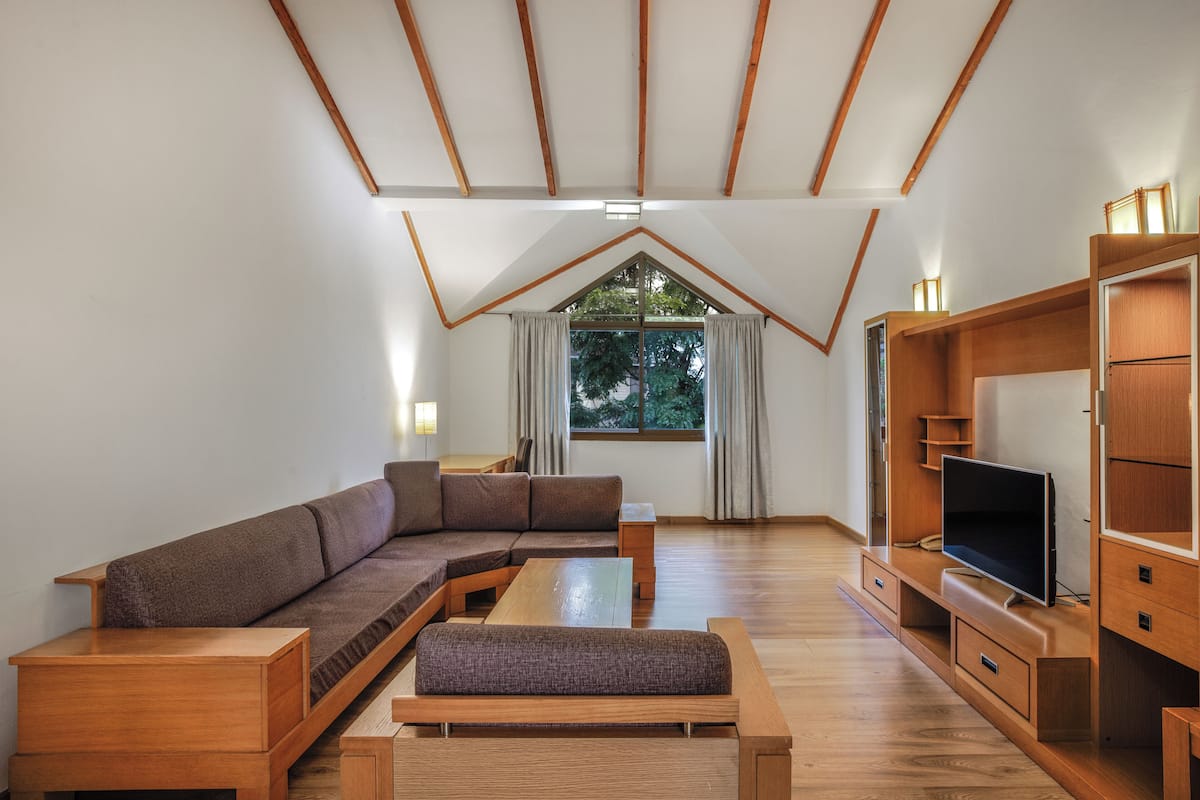 Uma sala de estar moderna com teto de madeira, uma janela grande com cortinas, um sofá modular, uma TV e móveis de madeira.